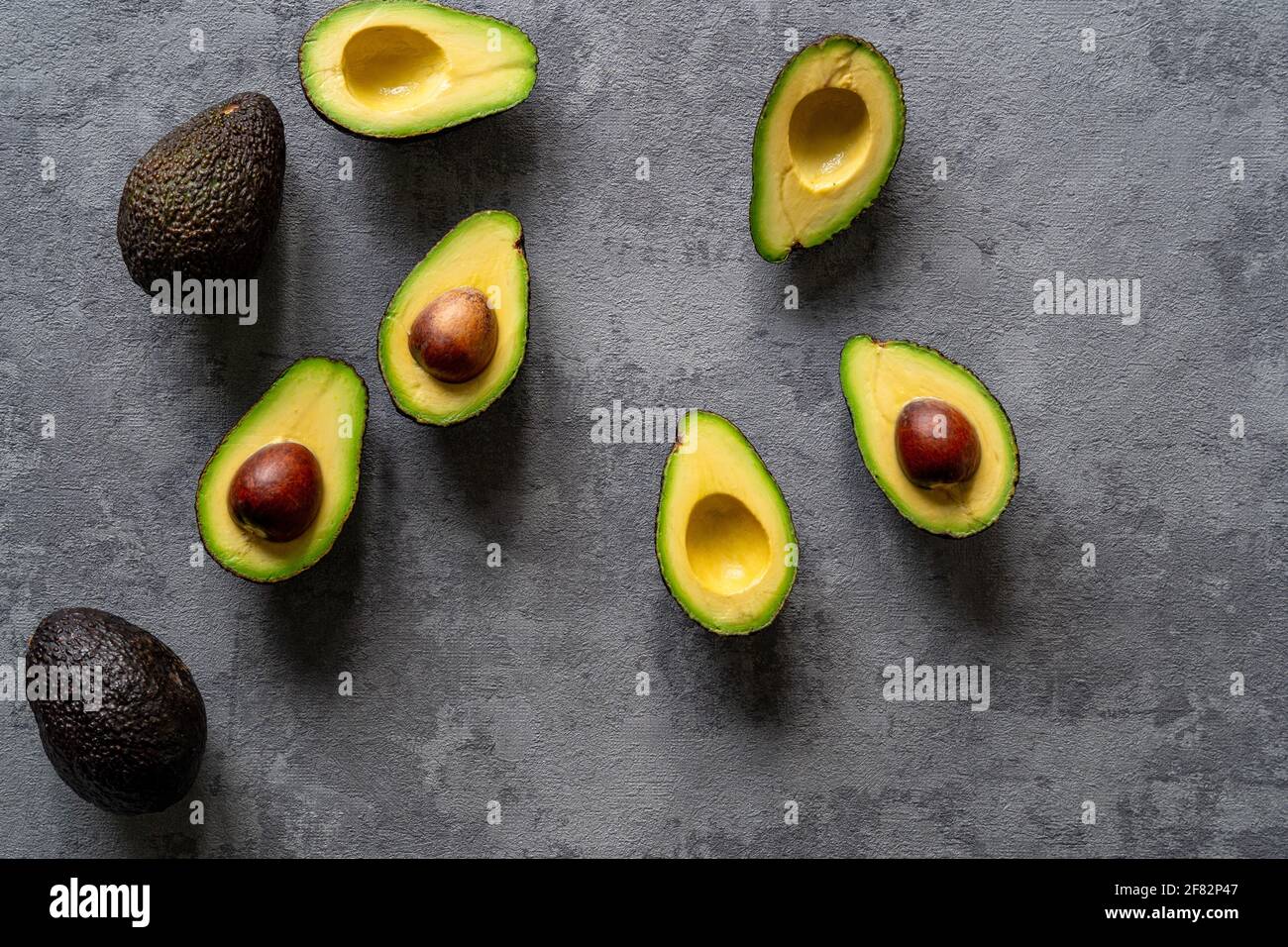 A creative top view of sliced and whole avocados on a textured grey ...