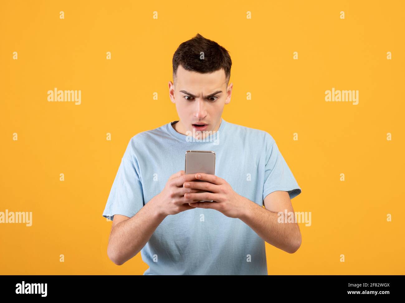 Handsome young guy staring at mobile phone in shock over orange studio ...