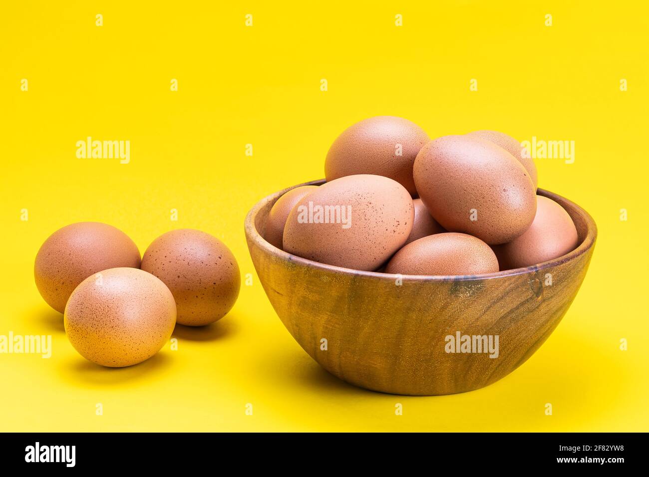 Side view of fresh chicken eggs in wooden bowl and on yellow background ...