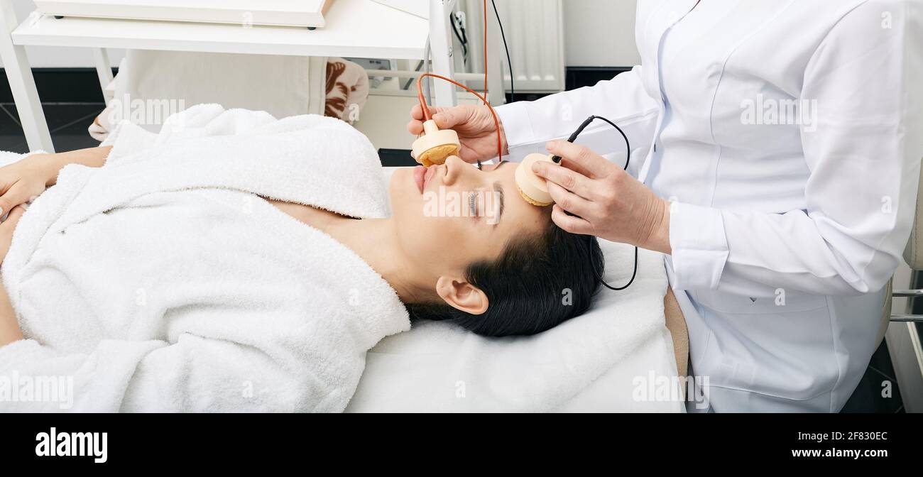 Beautiful brunette woman during facial microcurrent procedure for ...
