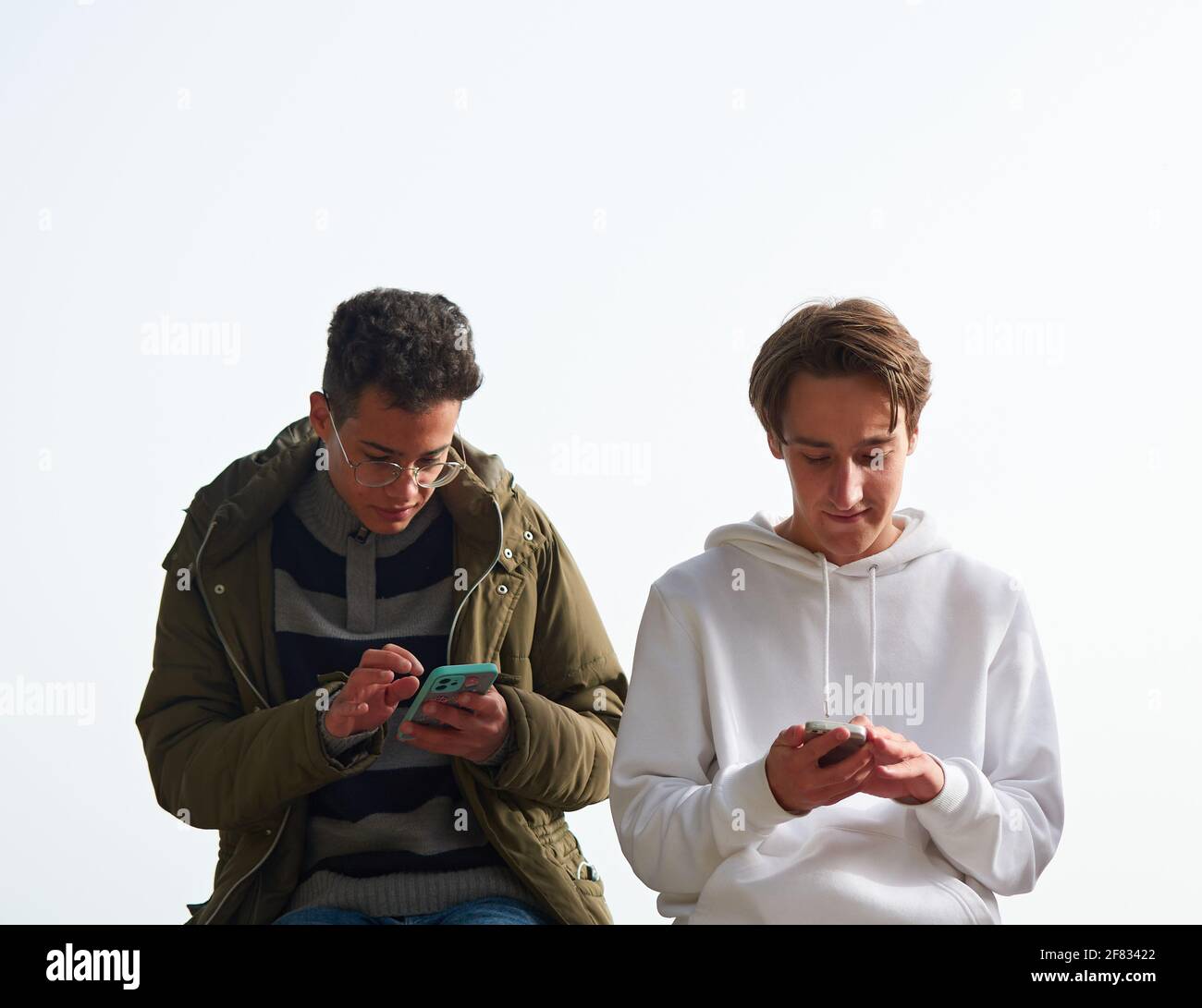 A closeup of two Caucasian and Hispanic guys using their smartphones ...