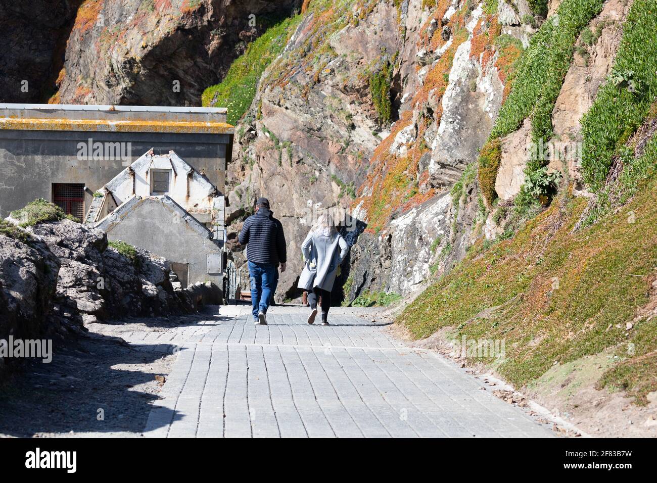 Two people walk down a steep hill at Lizard Point, Cornwall, UK Stock ...