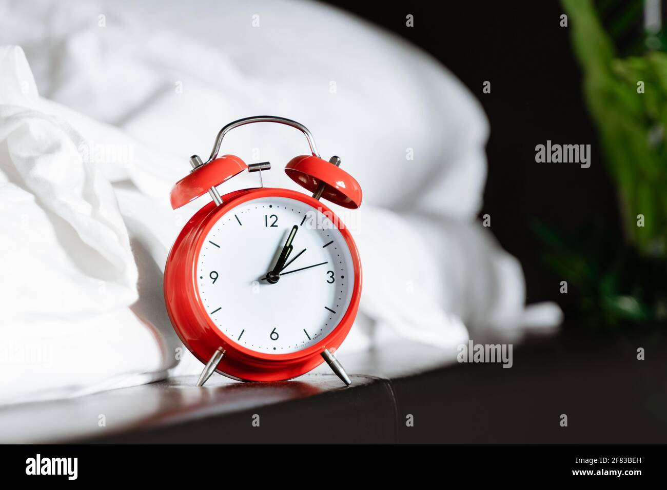 red retro alarm clock near nightstand at bed with white blanket sheet ...