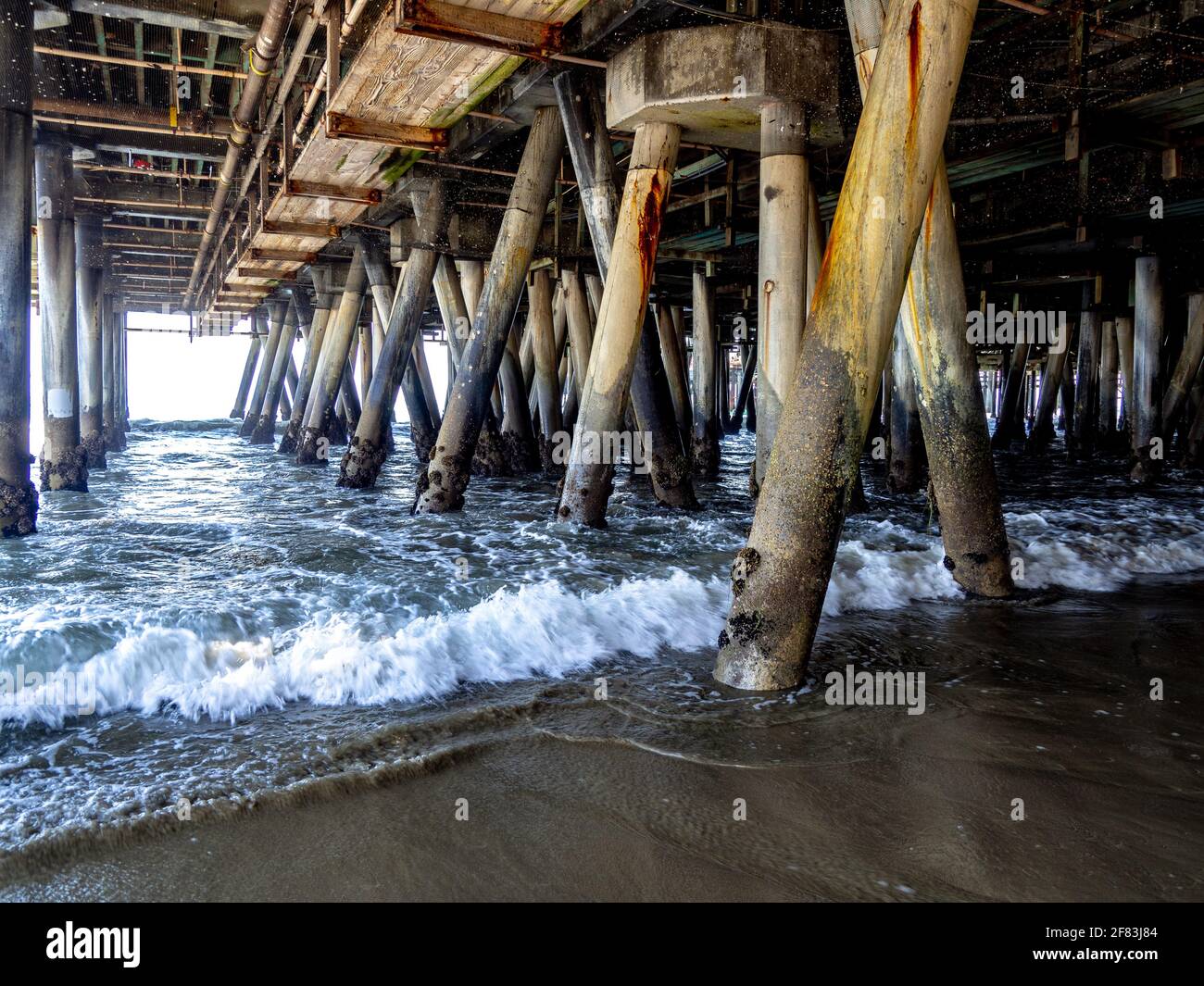 View of under a pier with waves and sand in summer Stock Photo - Alamy