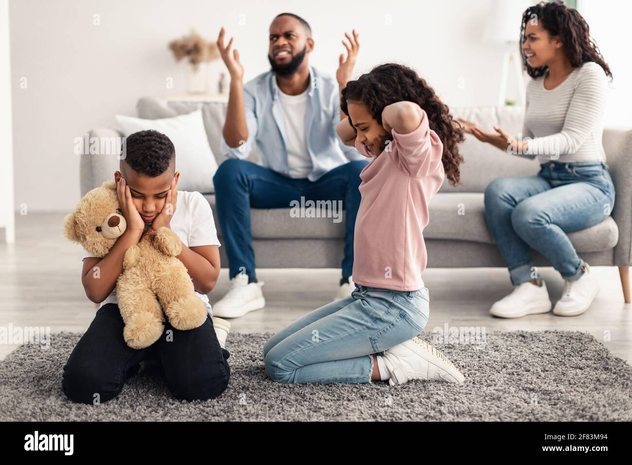 Upset black children covering ears, parents arguing in the background ...