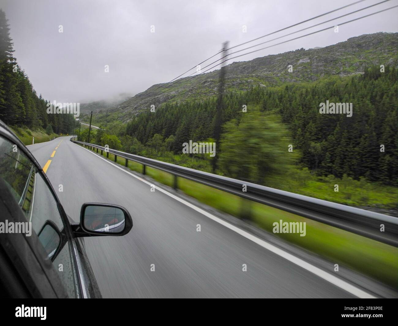 A view through car's window going across road running along hills with ...