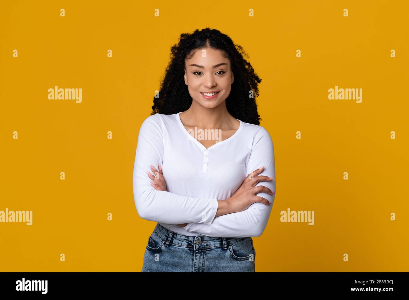 Young black confident lady posing with folded arms over yellow ...