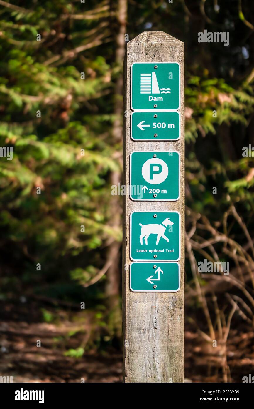 Trail sign on wood post in front of trees. Multiple small placards with ...
