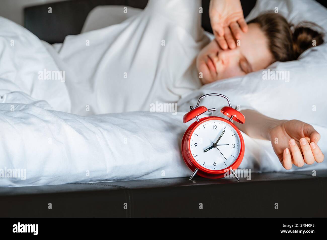 sleepy young millennial woman waking up in white bed yawning rubbing ...