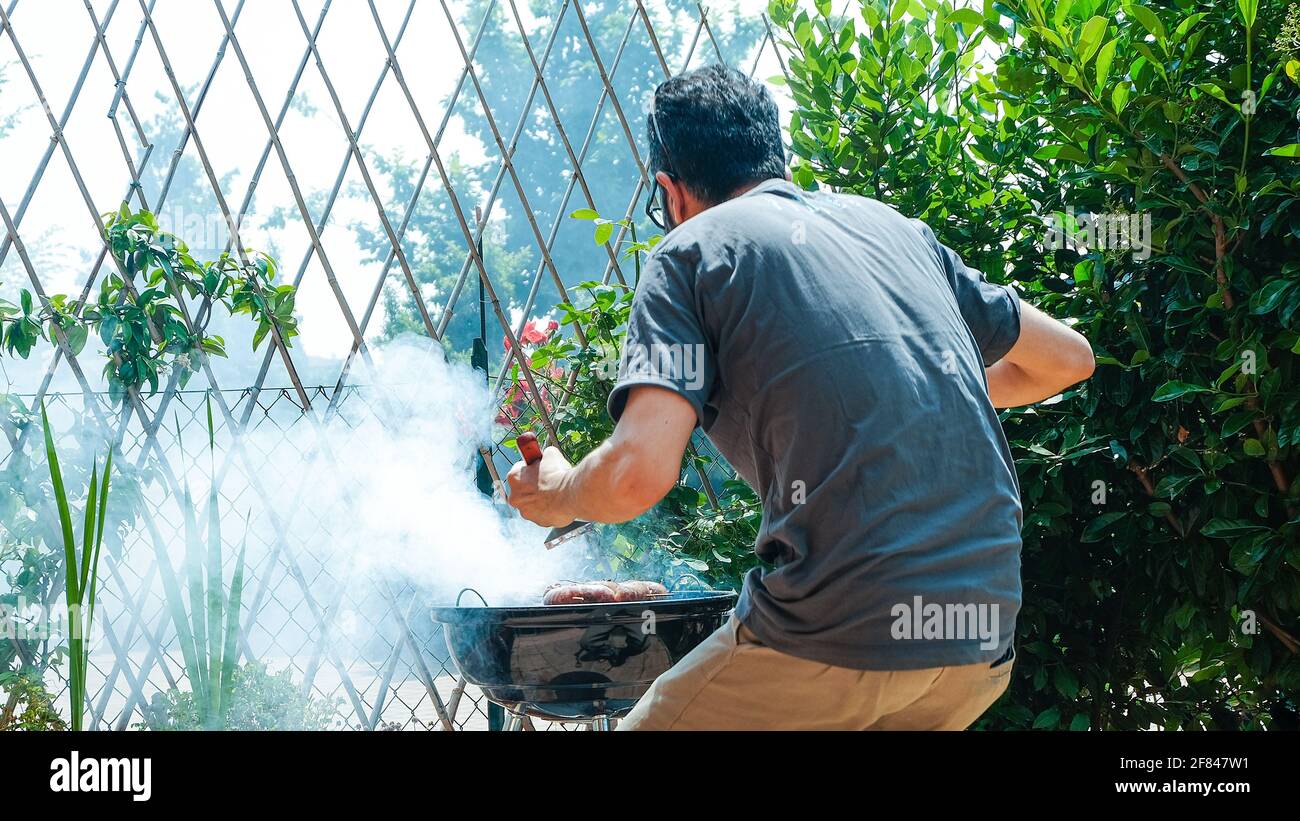A back view of a person grilling the sausages on the charcoal grill in ...