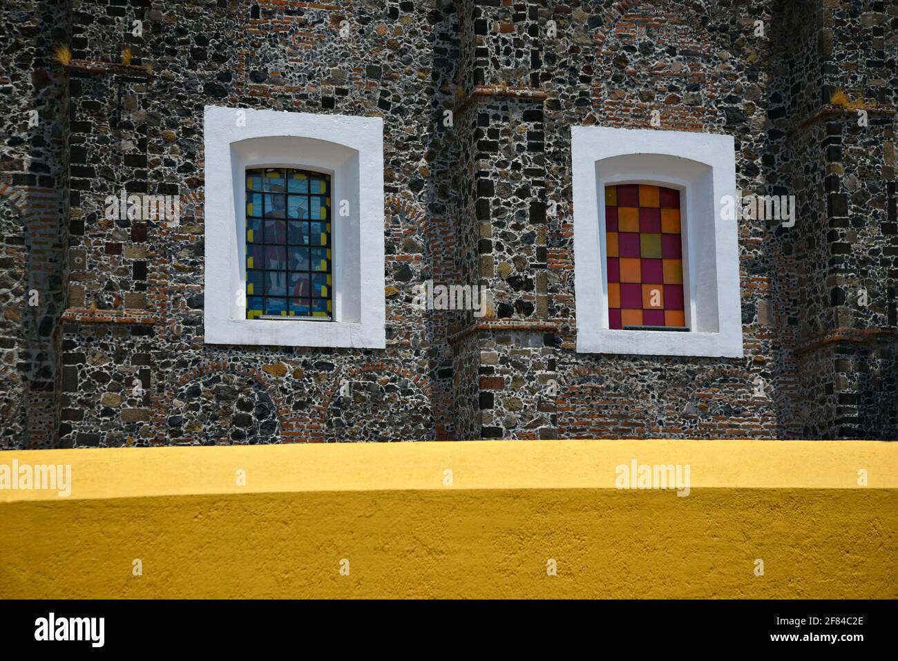 Stained glass windows with white trim on the ochre and stone wall of ...
