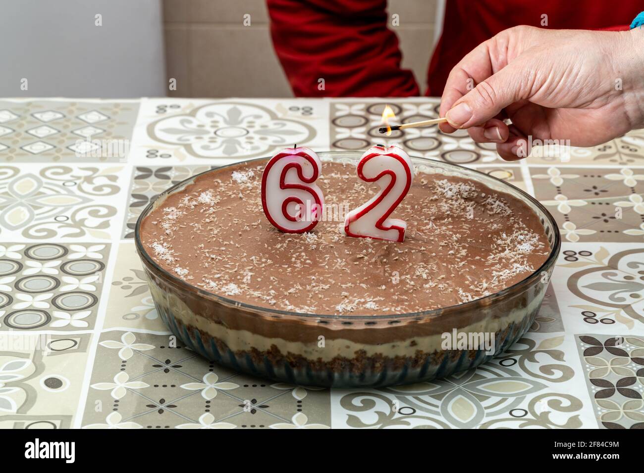 A chocolate birthday cake with a match lighting candles for a 62-year ...