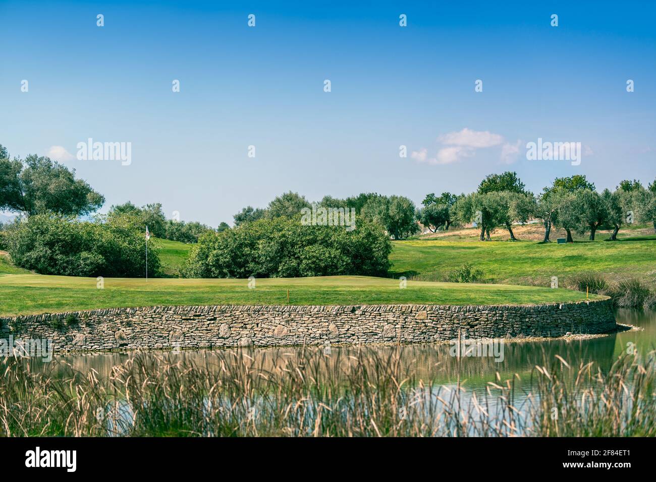 Golf course green with water hazard and stone wall Stock Photo - Alamy