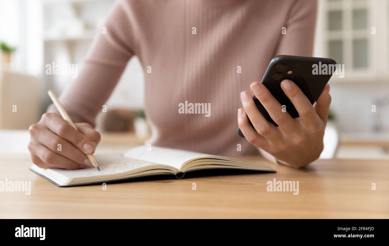 Young lady using smartphone write up information from online sources ...