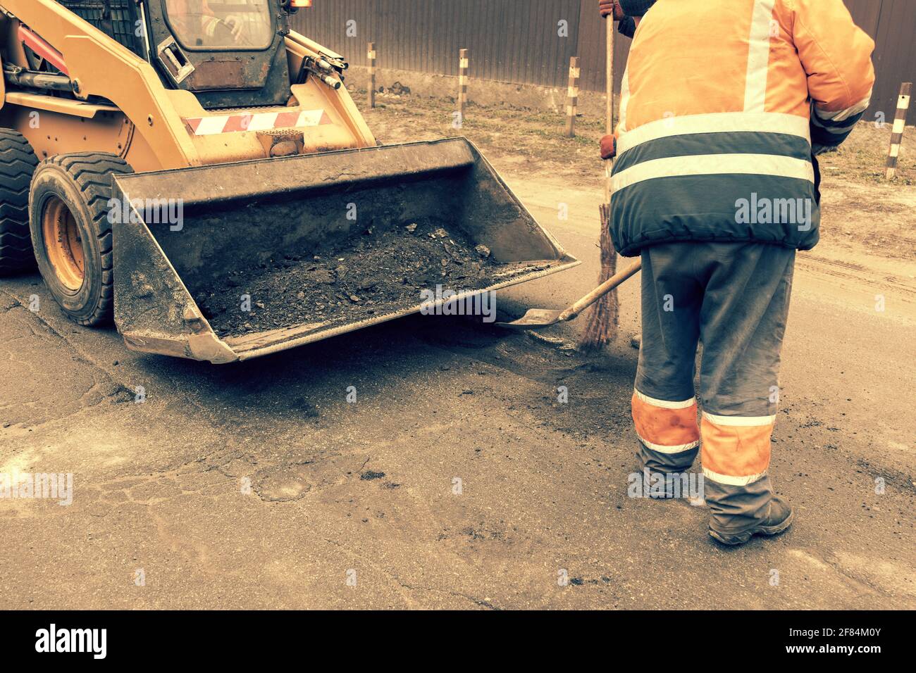 Road workers in bright orange reflective uniforms use shovels to scrape ...