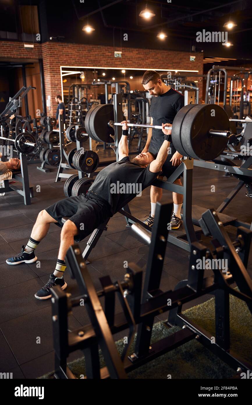 Hard-working man lifting weights with his friend back-up Stock Photo ...