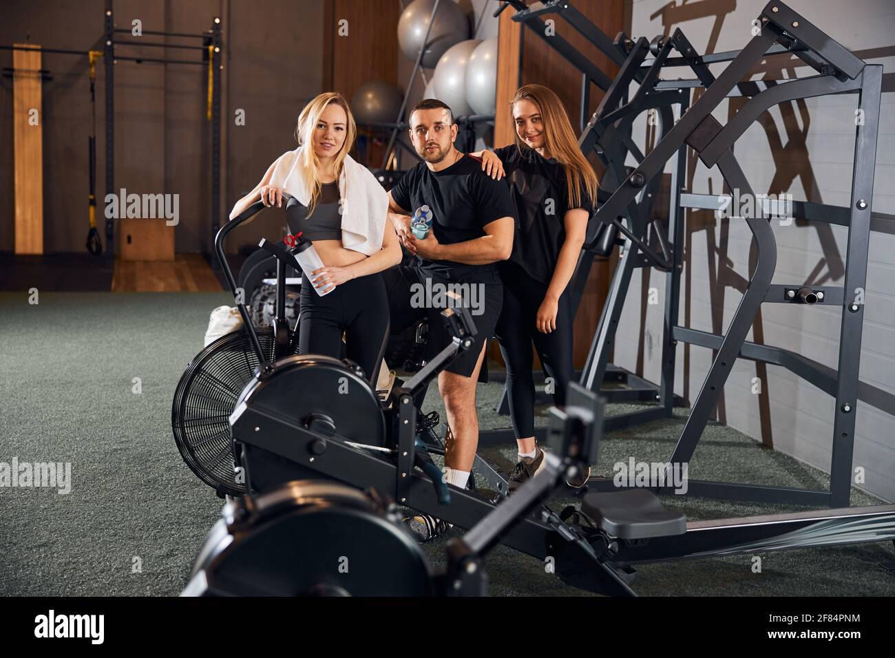 Three athletic young people with sports equipment posing for camera ...