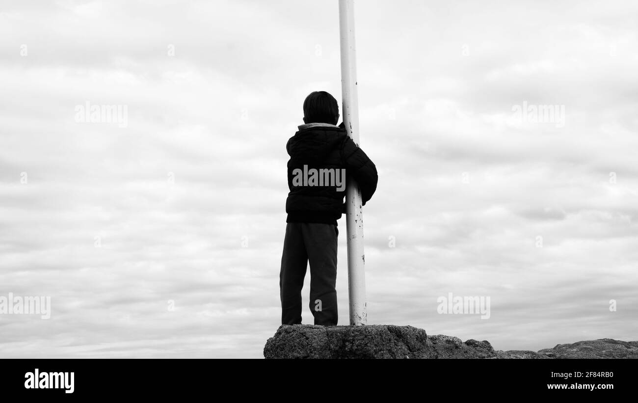 A grayscale shot of a child hugging a pole under a cloudy sky Stock ...