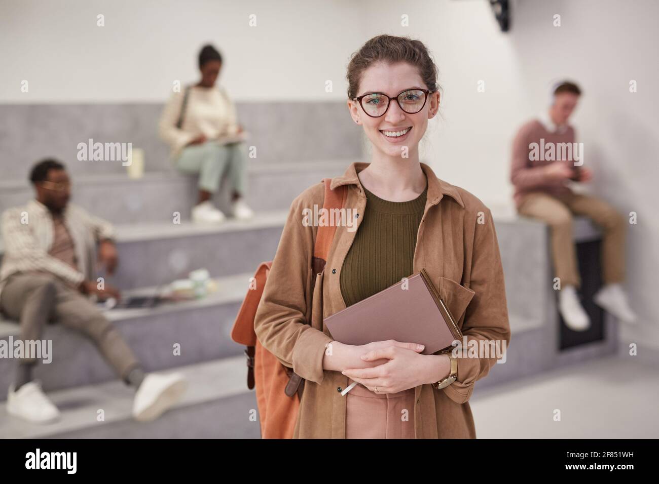 Waist up portrait of smiling female student looking at camera while ...