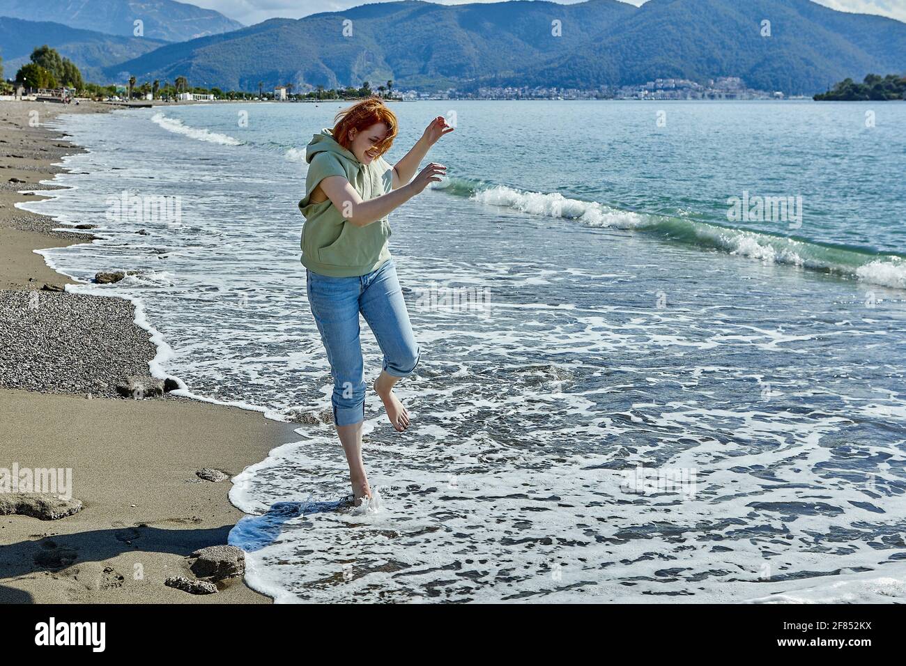 Barefoot young woman tries to walk on cool water in surf zone in early ...