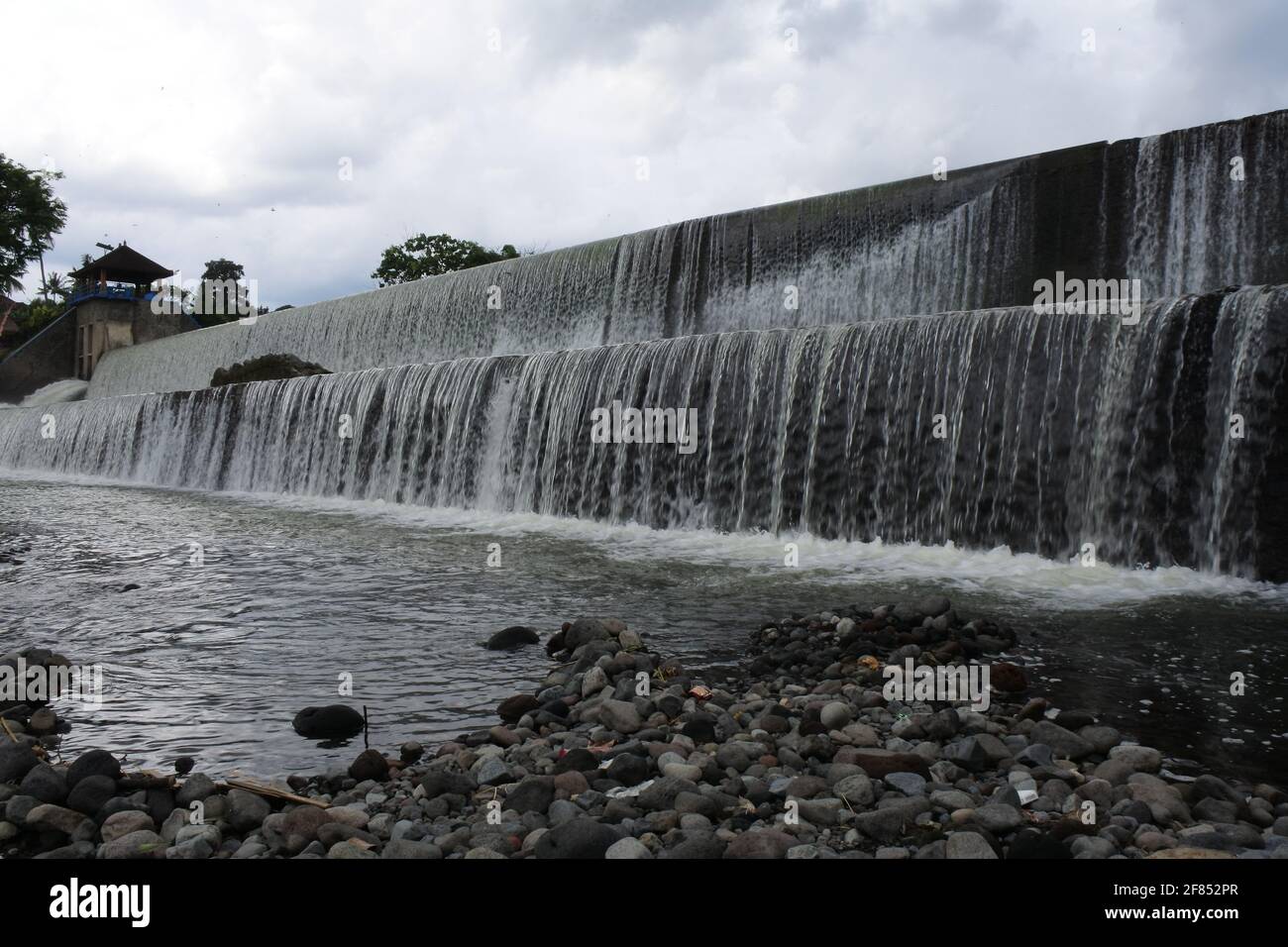 a two-story waterfall with little pebbles on the shore under a cloudy ...