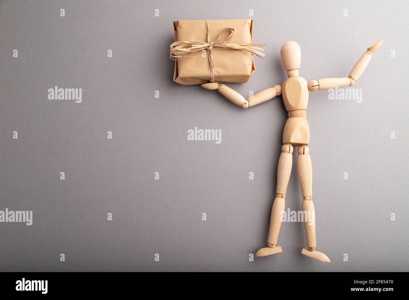 Wooden mannequin holding a gift box on gray pastel background. copy ...