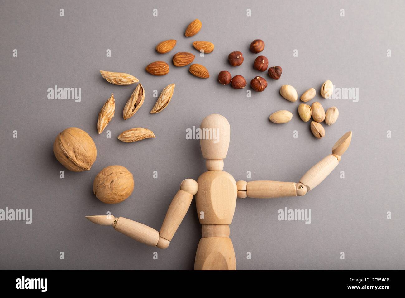Wooden mannequin juggling nuts on gray pastel background. close up ...