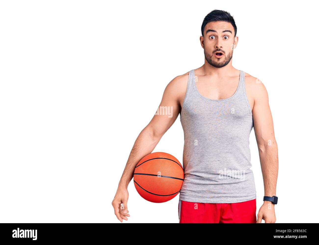 Young handsome man holding basketball ball scared and amazed with open ...