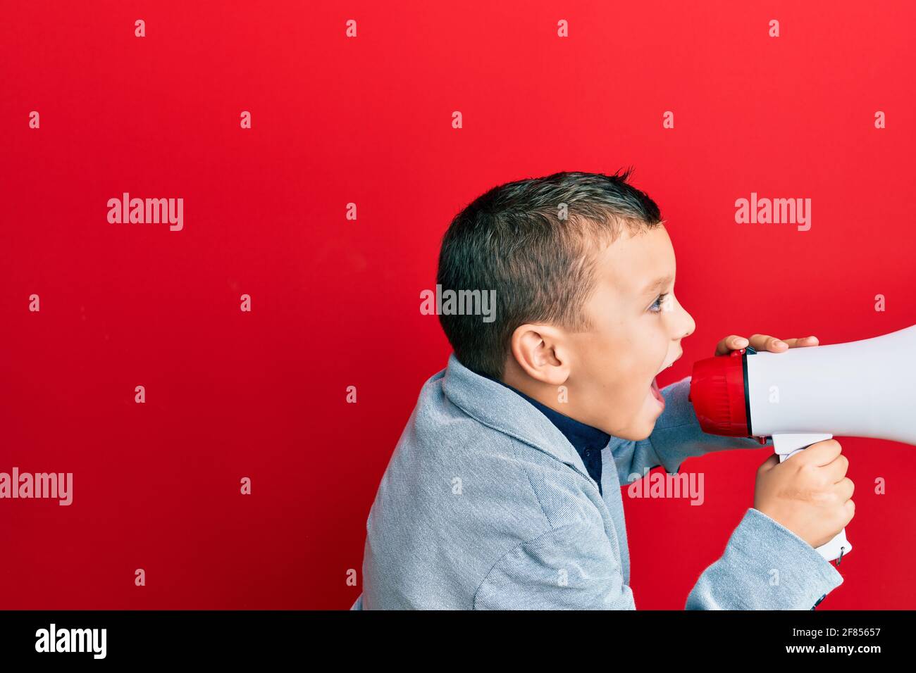 Adorable caucasian boy screaming using megaphone over isolated red ...