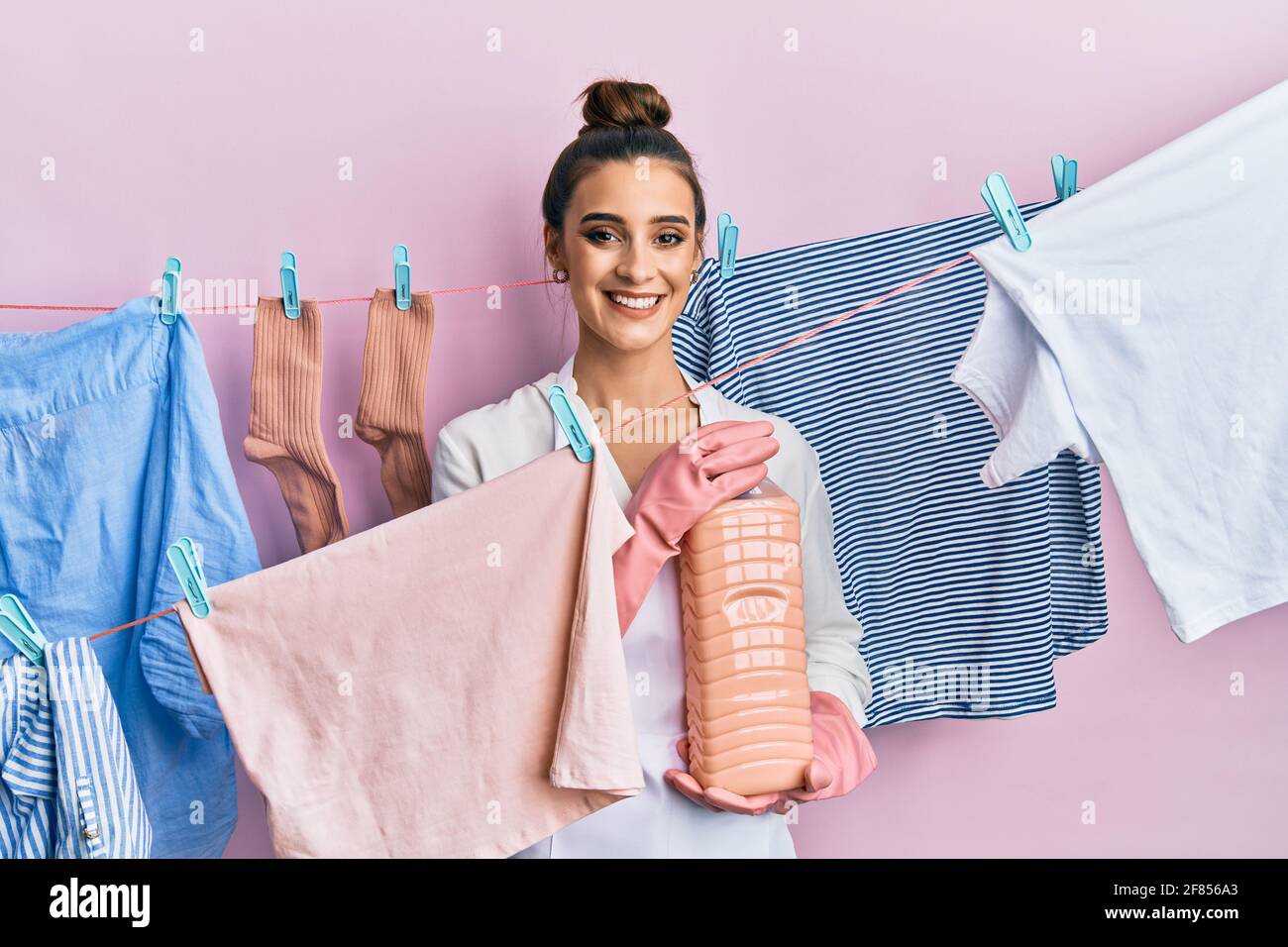 Beautiful brunette young woman doing laundry holding detergent bottle ...