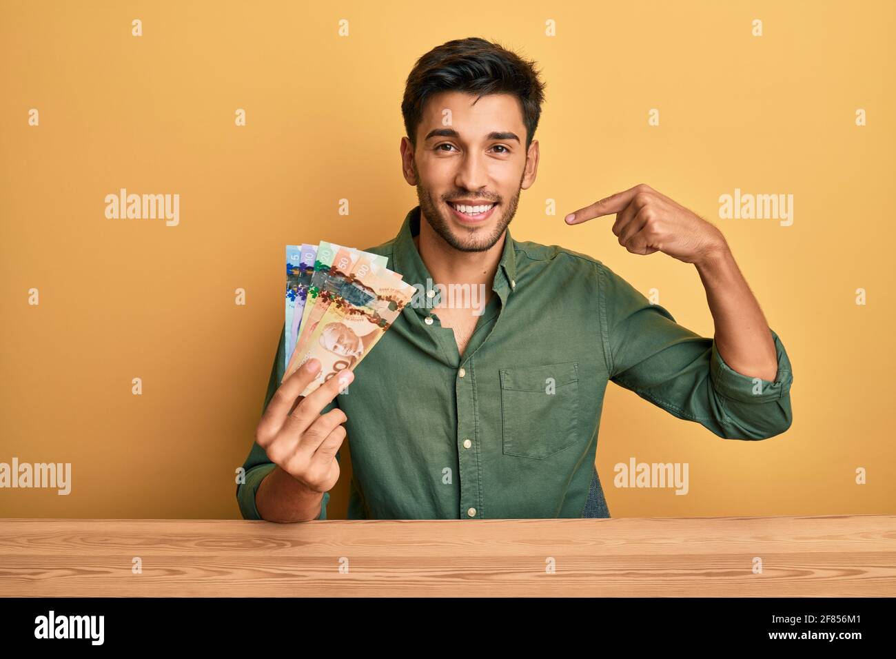 Young handsome man holding canadian dollars looking confident with ...