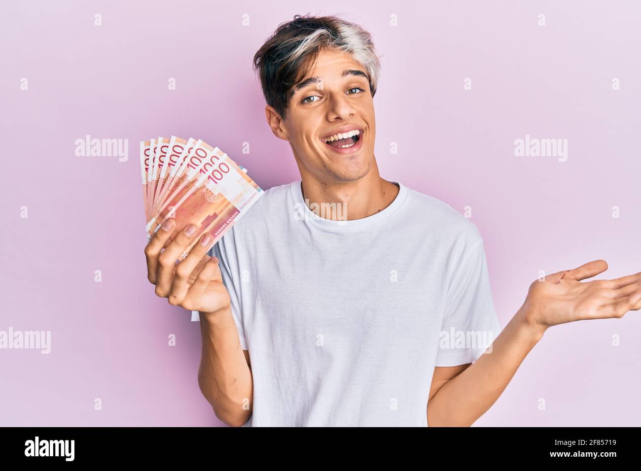 Young hispanic man holding 100 norwegian krone banknotes celebrating ...