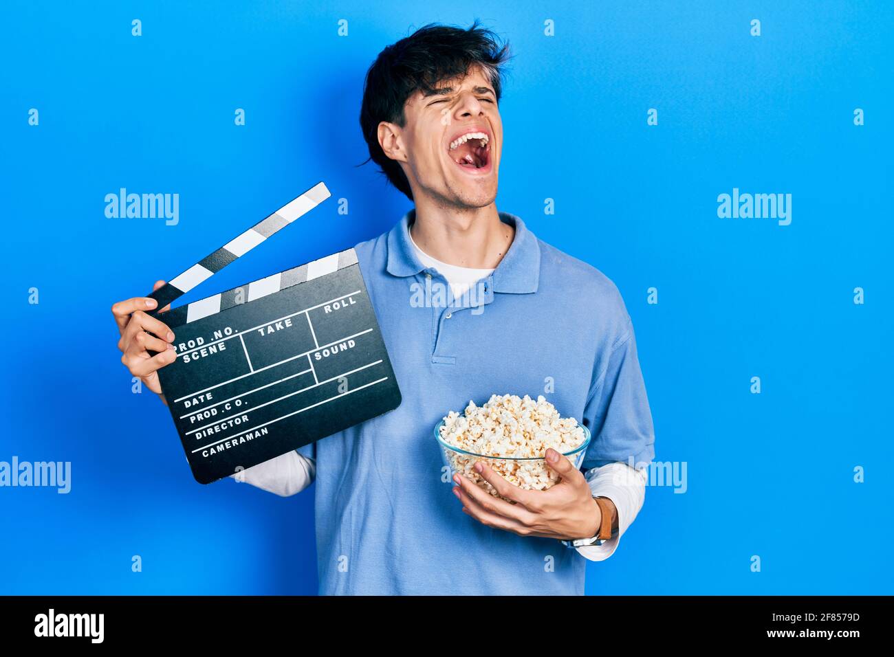 Handsome hipster young man eating popcorn holding cinema clapboard ...