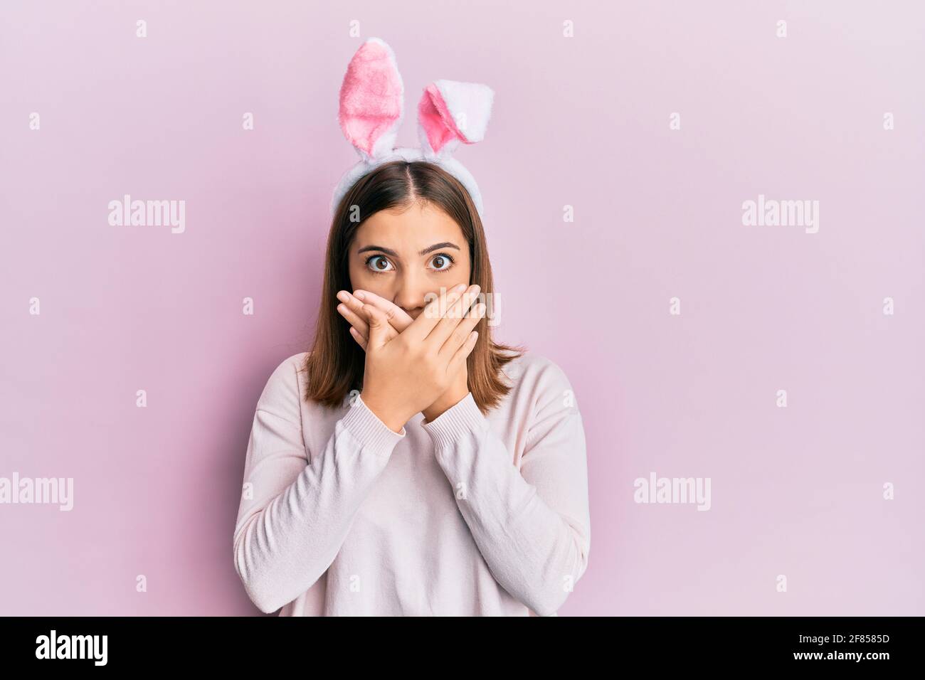 Young beautiful woman wearing cute easter bunny ears shocked covering ...