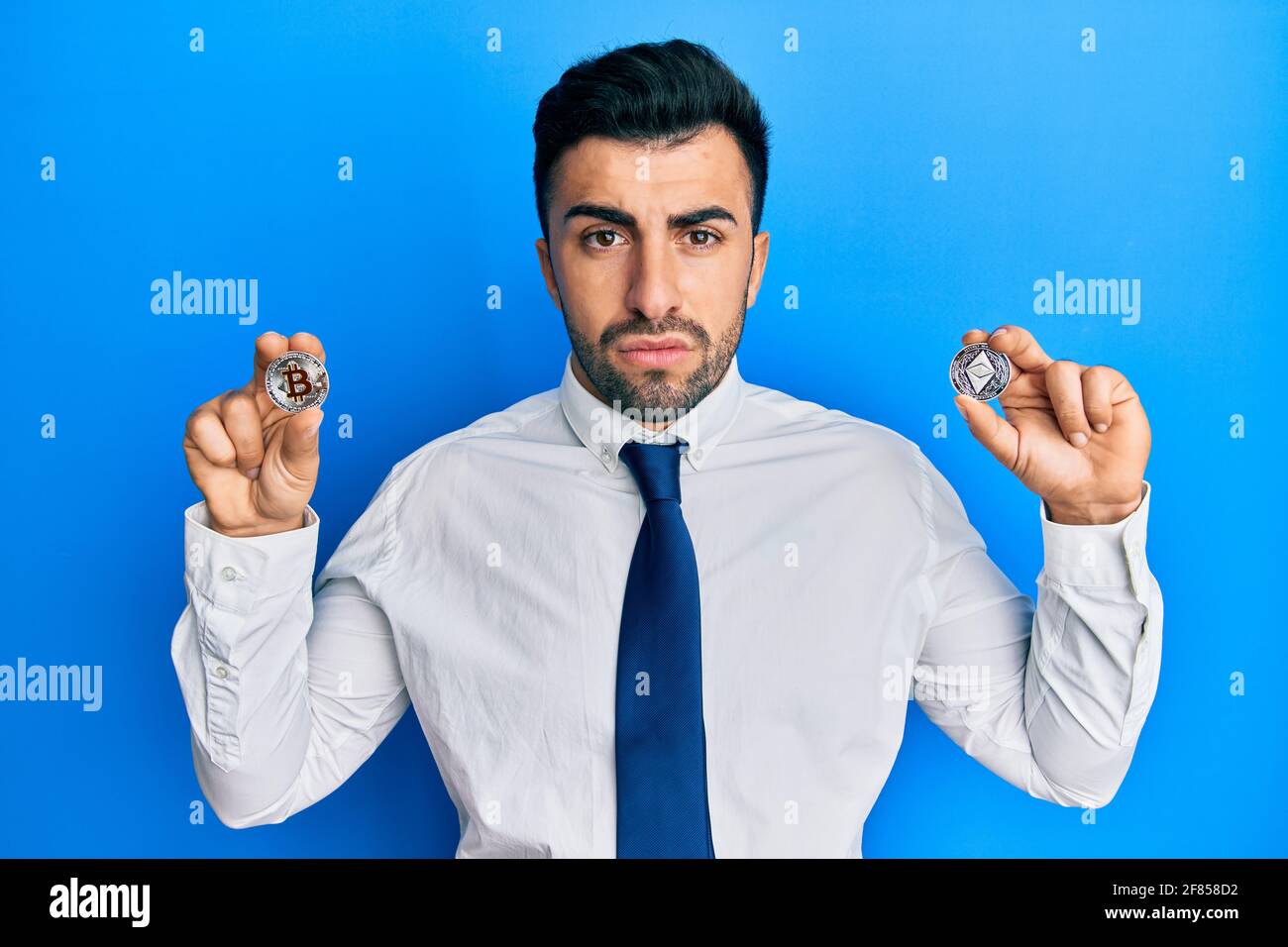 Young hispanic man holding virtual currency ethereum coin and bitcoin ...