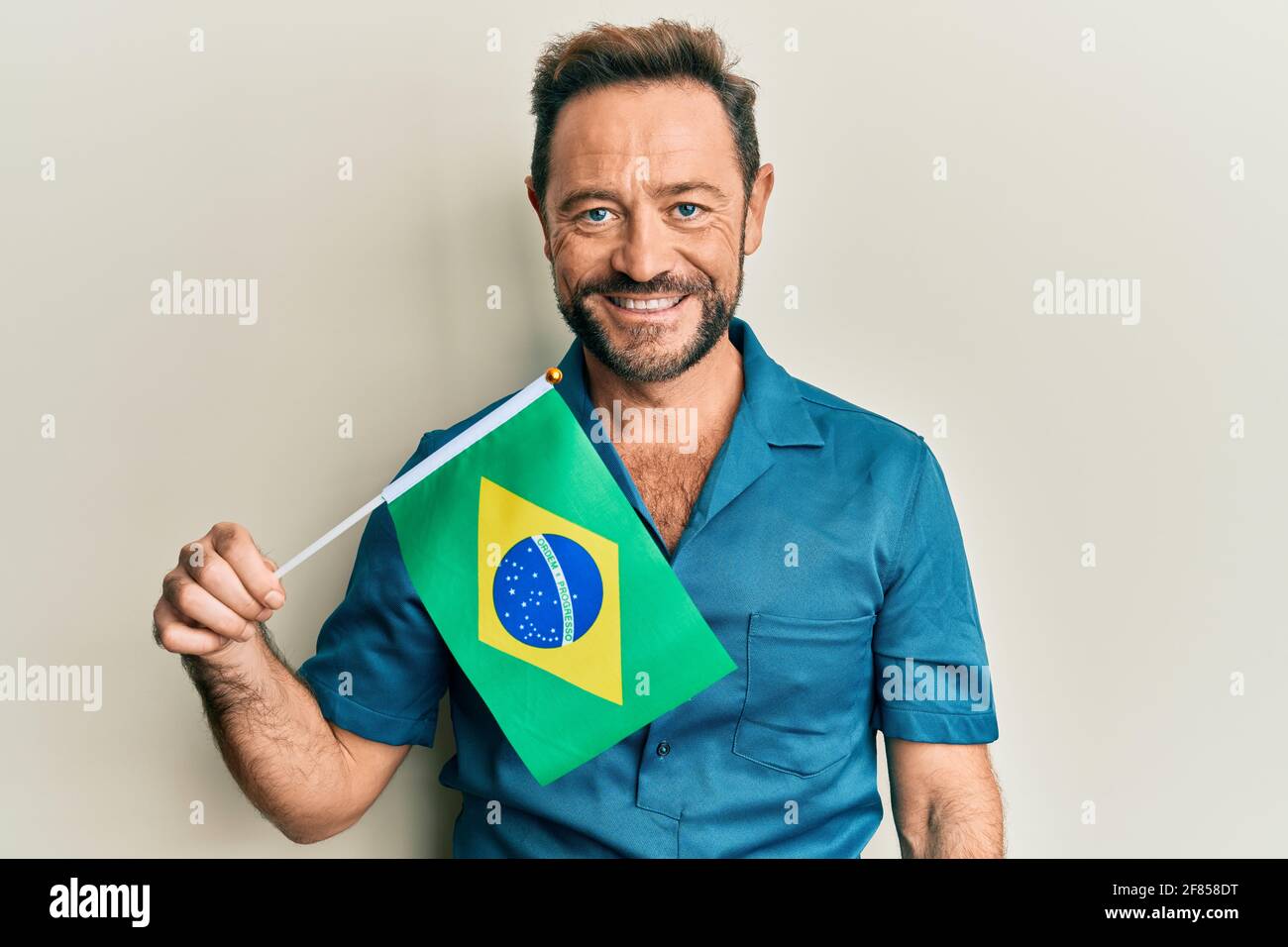 Middle age man holding brazil flag looking positive and happy standing ...