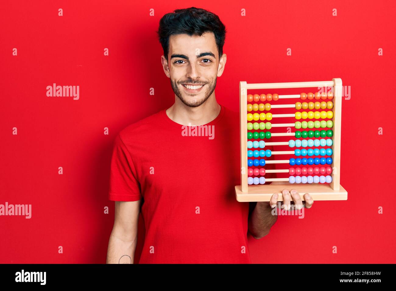 Young hispanic man holding traditional abacus looking positive and ...