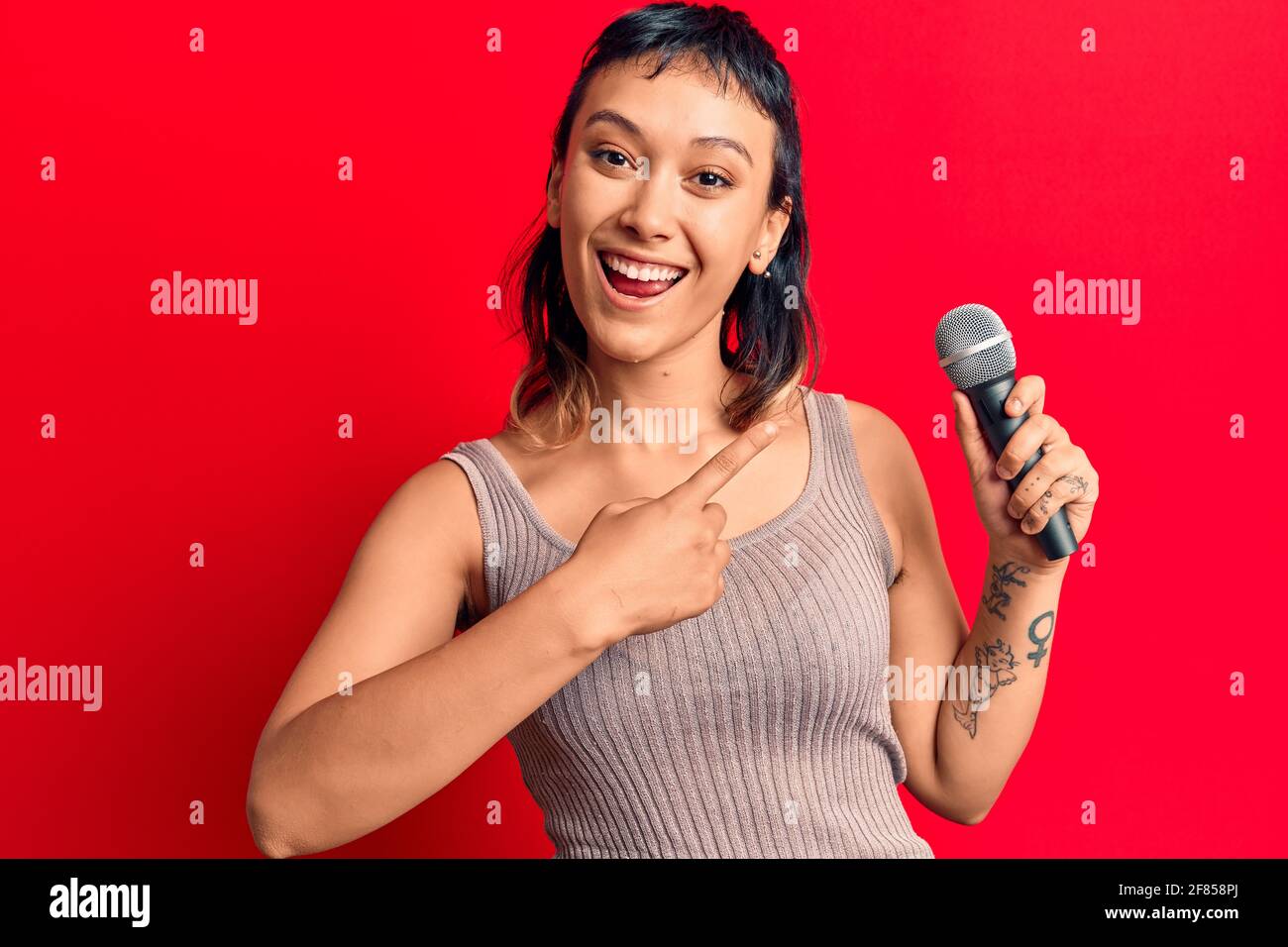 Young woman singing song using microphone smiling happy pointing with ...