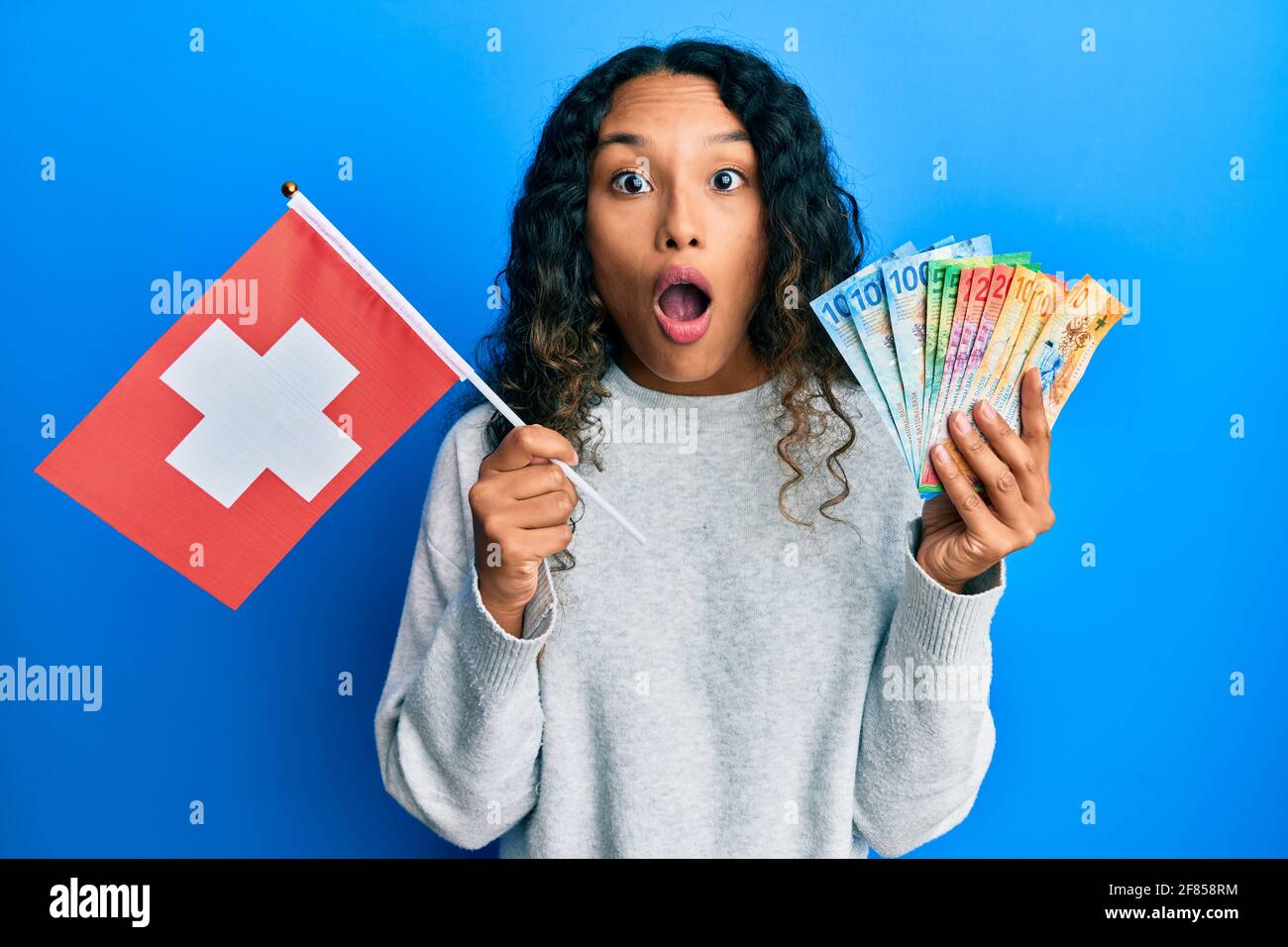 Young latin woman holding switzerland flag and swiss franc banknotes ...