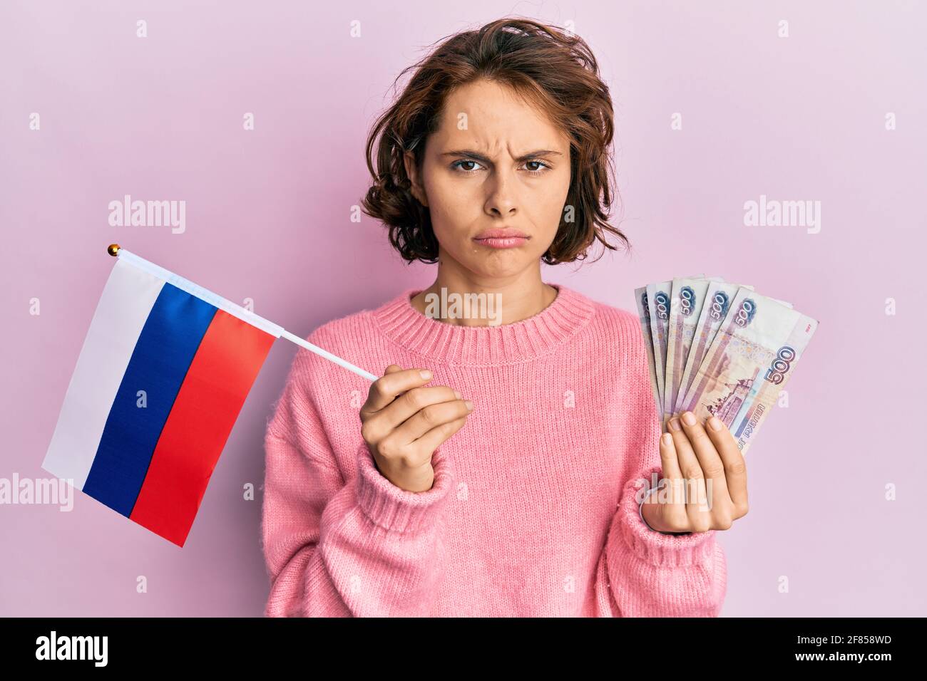 Young brunette woman holding russia flag and rubles banknotes depressed ...