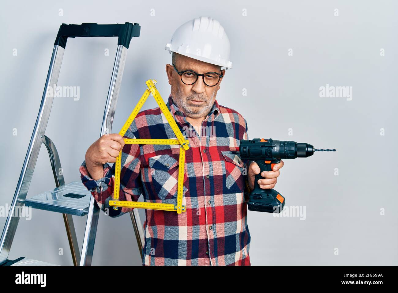 Handsome mature handyman holding screwdriver wearing hardhat by ...