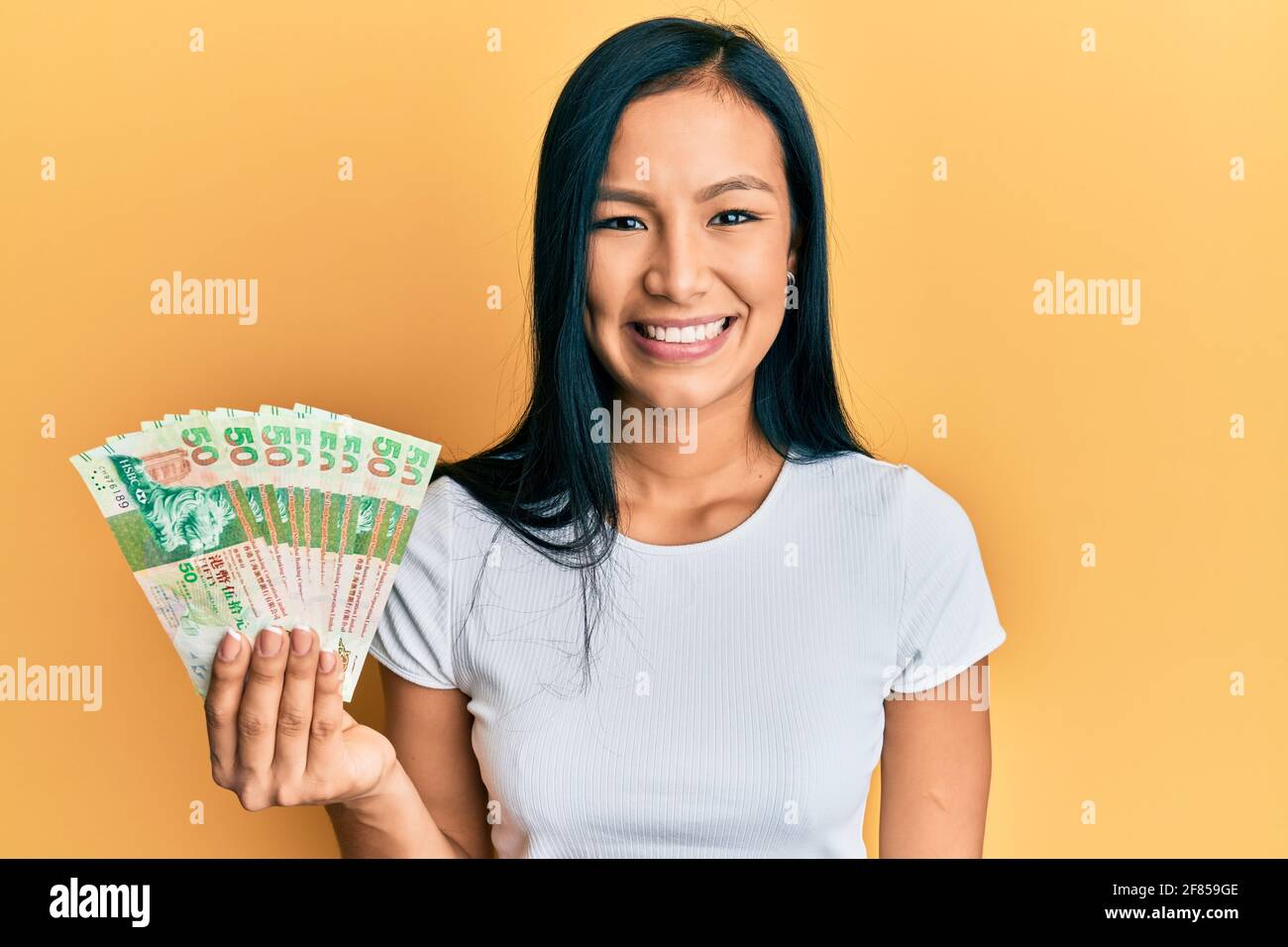 Beautiful hispanic woman holding hong kong 50 dollars banknotes looking ...