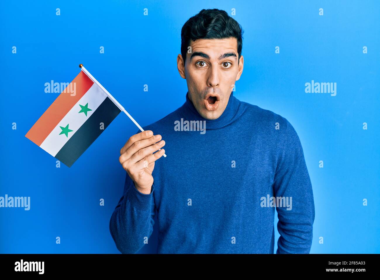 Handsome hispanic man holding syria flag scared and amazed with open ...