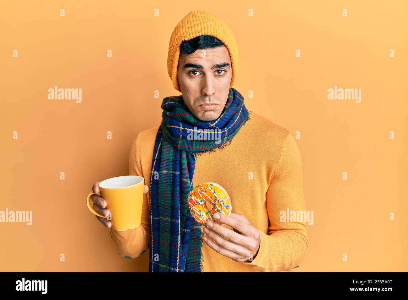 Handsome hispanic man eating doughnut and drinking coffee depressed and ...