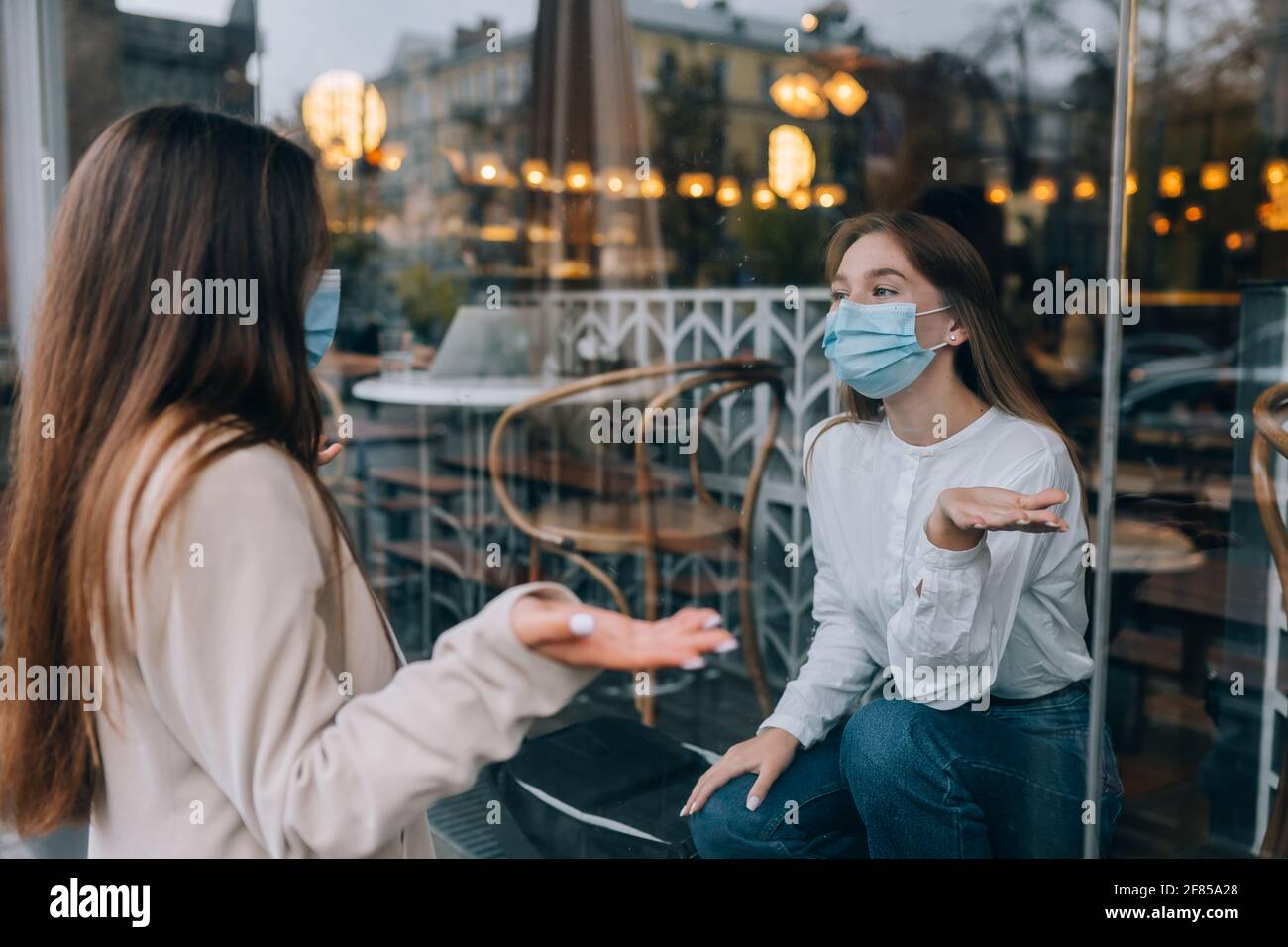 Two women in protective masks opposite each other, window between them ...