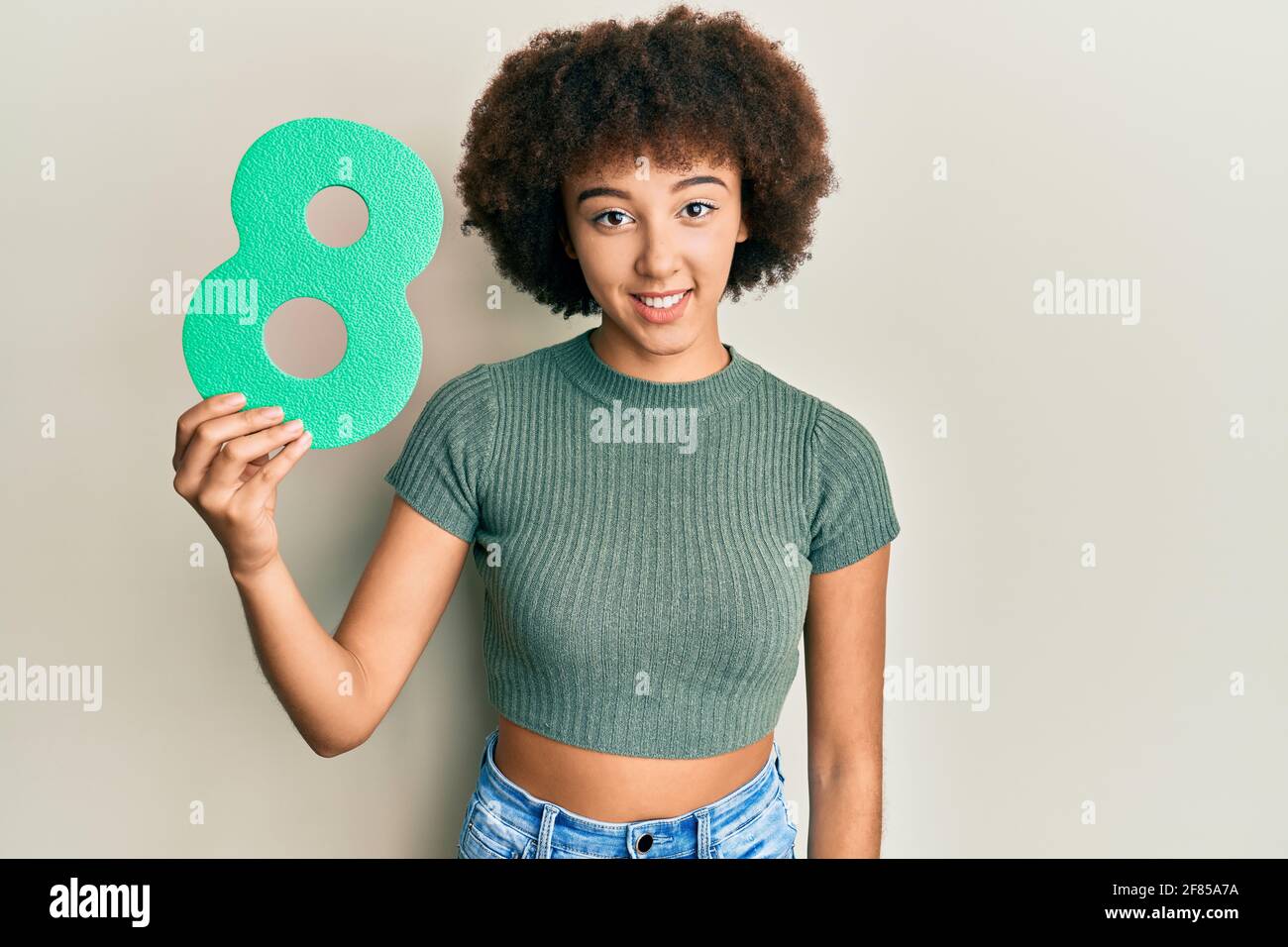 Young hispanic girl holding number eight looking positive and happy ...