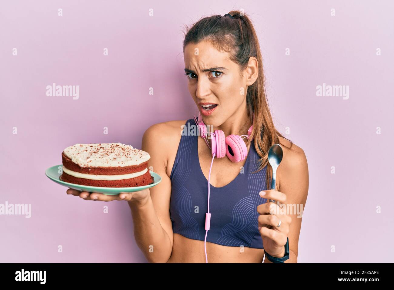 Young beautiful woman wearing gym clothes holding carrot cake clueless ...