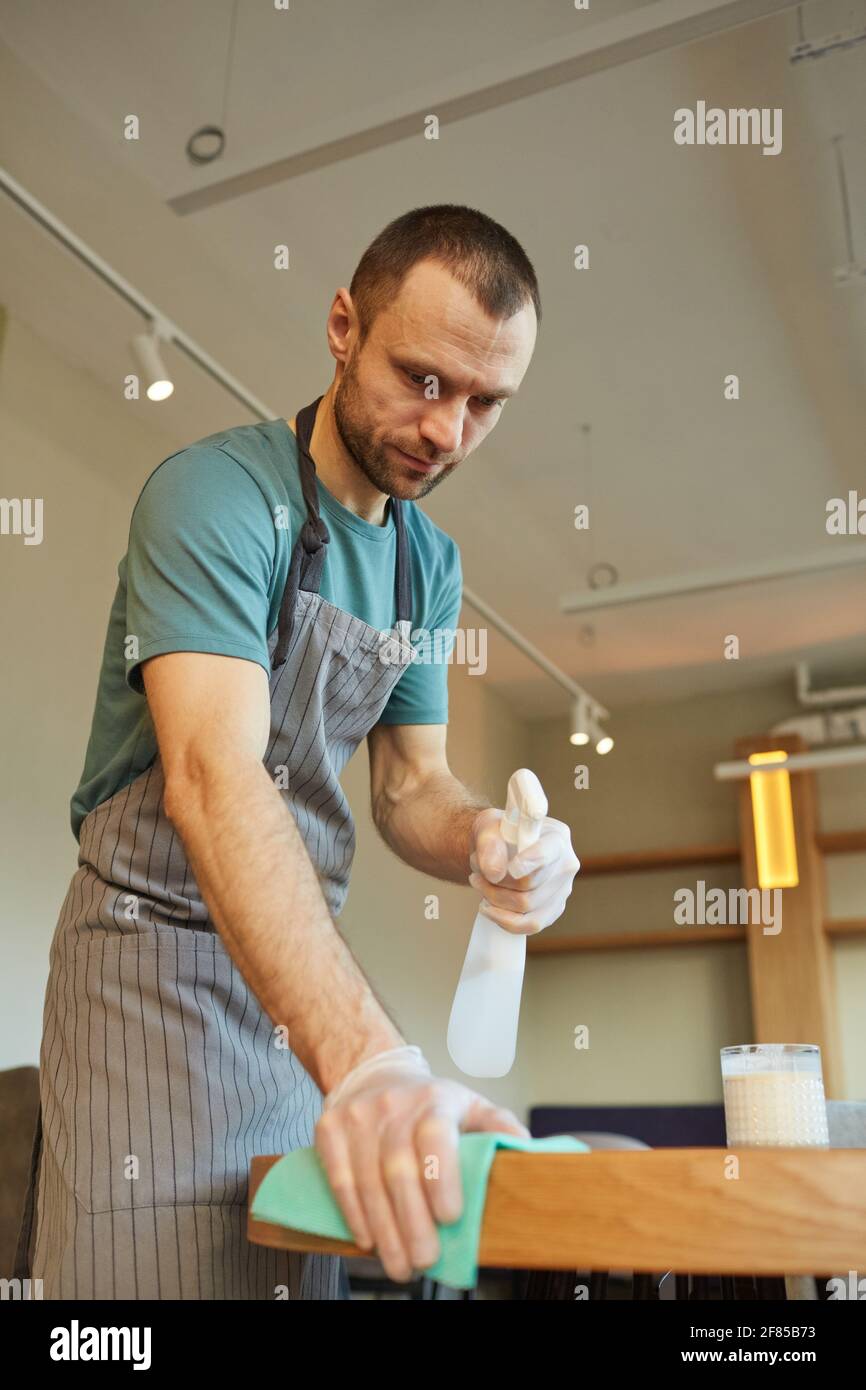 Vertical warm toned portrait of male waiter cleaning table in coffee ...