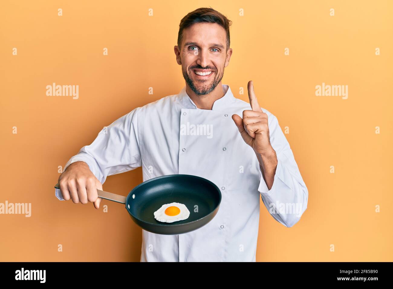 Handsome man with beard professional chef cooking fried egg smiling ...