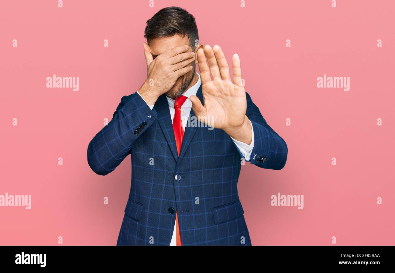 Handsome man with beard wearing business suit and tie covering eyes ...